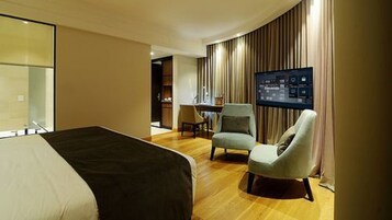 Quarto de hotel moderno com uma cama grande, uma escrivaninha, uma cadeira e uma televisão.