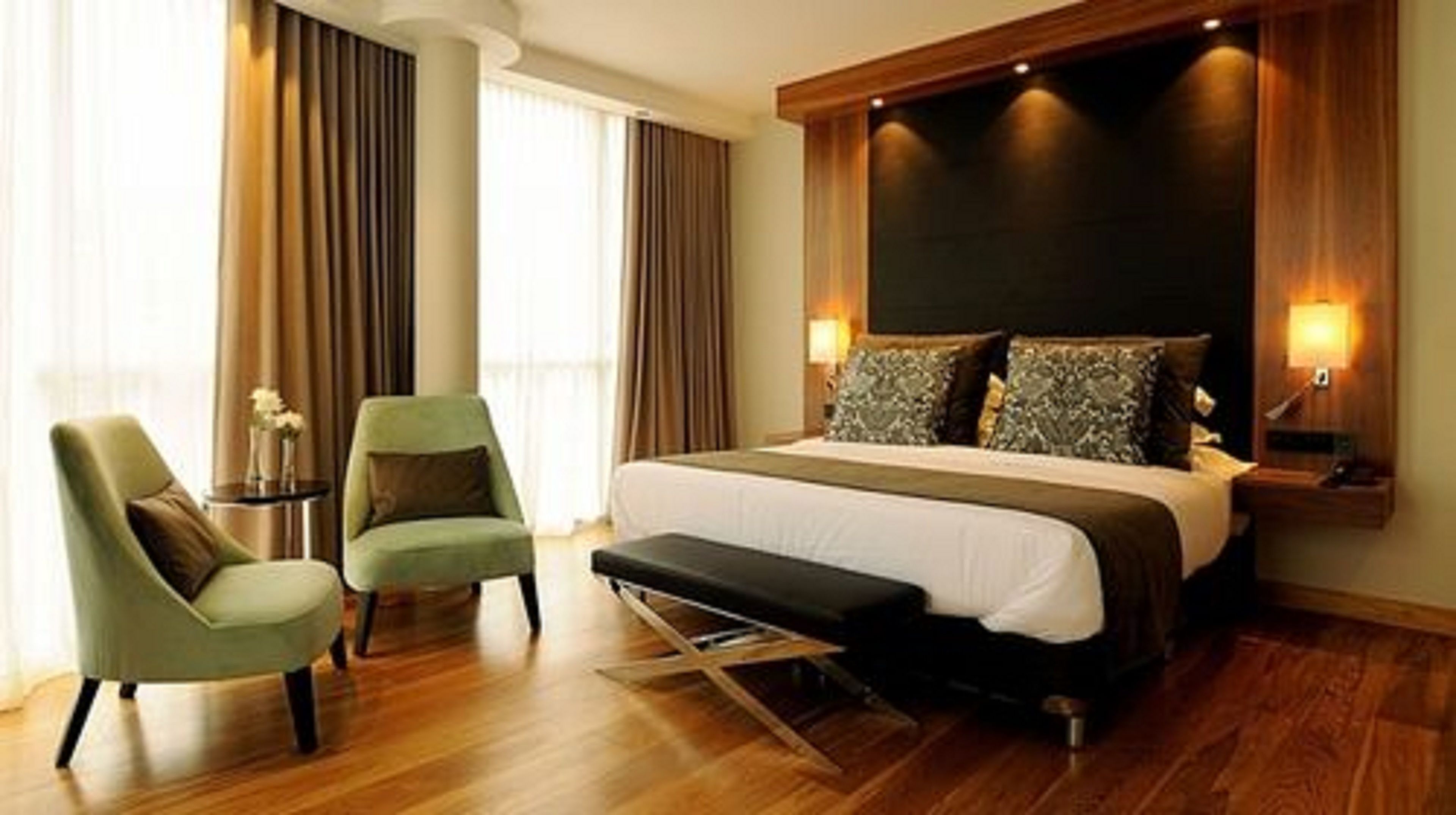 Quarto de hotel com uma cama grande, duas poltronas, uma mesa de cabeceira e um criado-mudo com abajur.