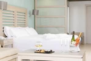 Quarto de hotel com cama, mesa de cabeceira com garrafa de champanhe, copos e bandeja de sobremesas.