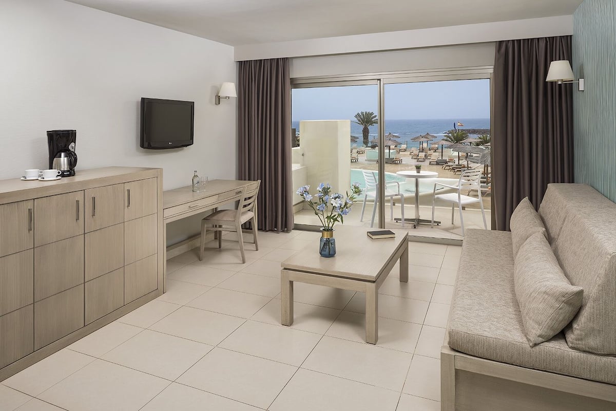 Quarto de hotel com cozinha compacta, área de jantar, sofá e varanda com vista para a piscina.