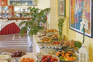 Buffet com diversos alimentos e uma grande planta em vaso.