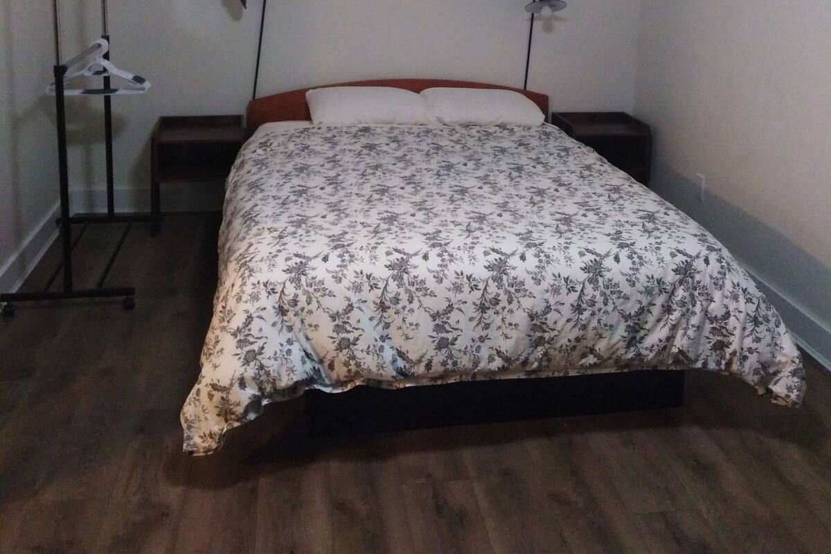 Quarto com cama, duas luminárias de cabeceira, um quadro na parede e um cabideiro.