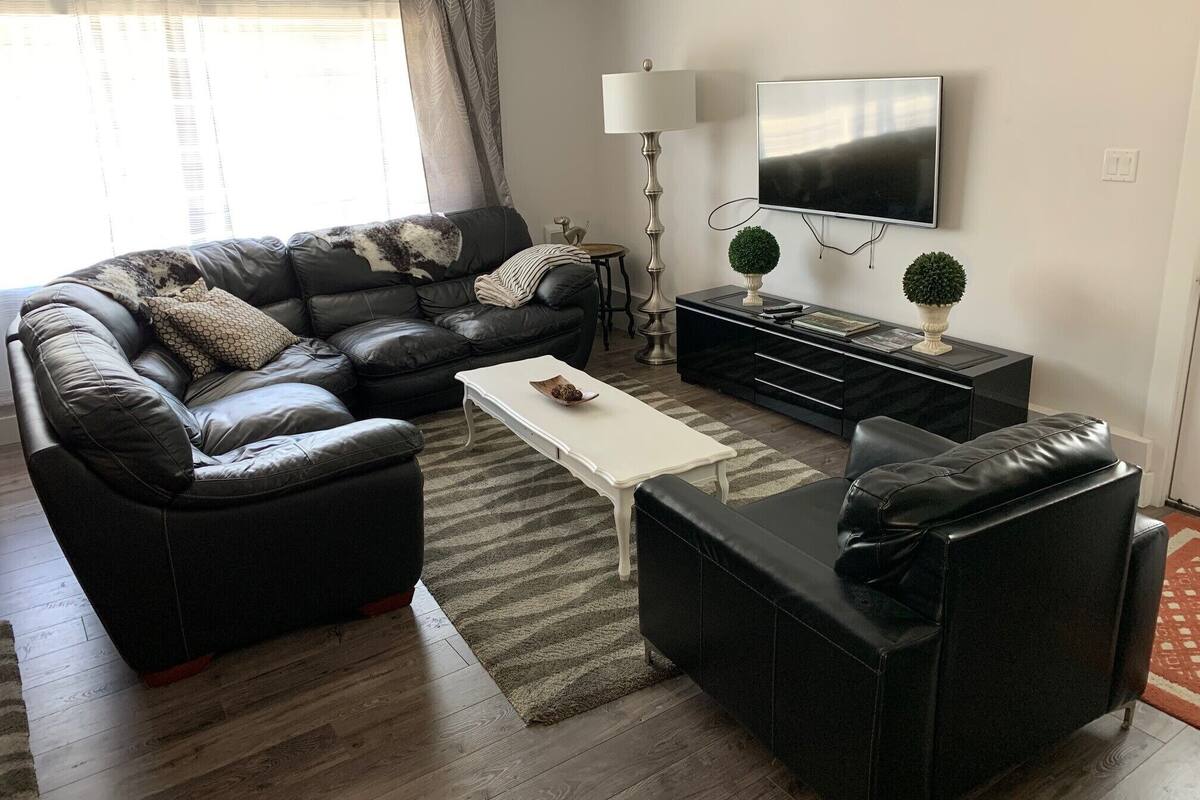 Uma sala de estar moderna com um sofá de couro, uma mesa de centro, uma televisão e uma mesinha lateral com objetos decorativos.