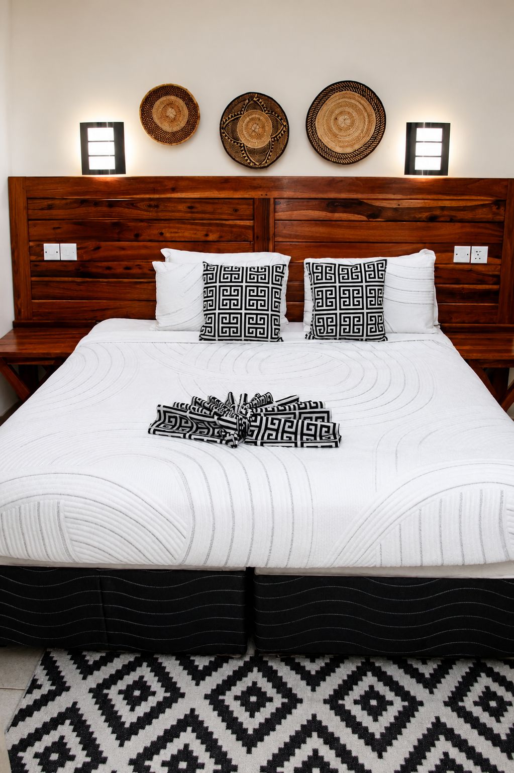 Cama bem arrumada com colcha estampada e almofadas, cabeceira de madeira e arte decorativa na parede.