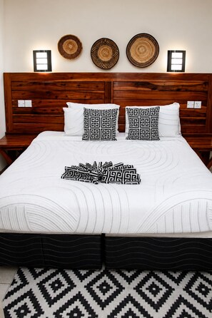 Cama bem arrumada com colcha estampada e almofadas, cabeceira de madeira e arte decorativa na parede.