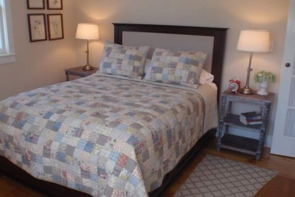 Quarto com uma cama grande, duas mesas de cabeceira com luminárias, um criado-mudo pequeno e uma porta.
