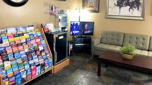 Uma sala de estar com sofá, mesa de centro, relógio, televisão e uma seleção de folhetos de viagem.