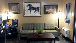 Uma sala de estar com um sofá cinza, uma mesa de centro com uma planta, uma televisão e quadros decorativos nas paredes.