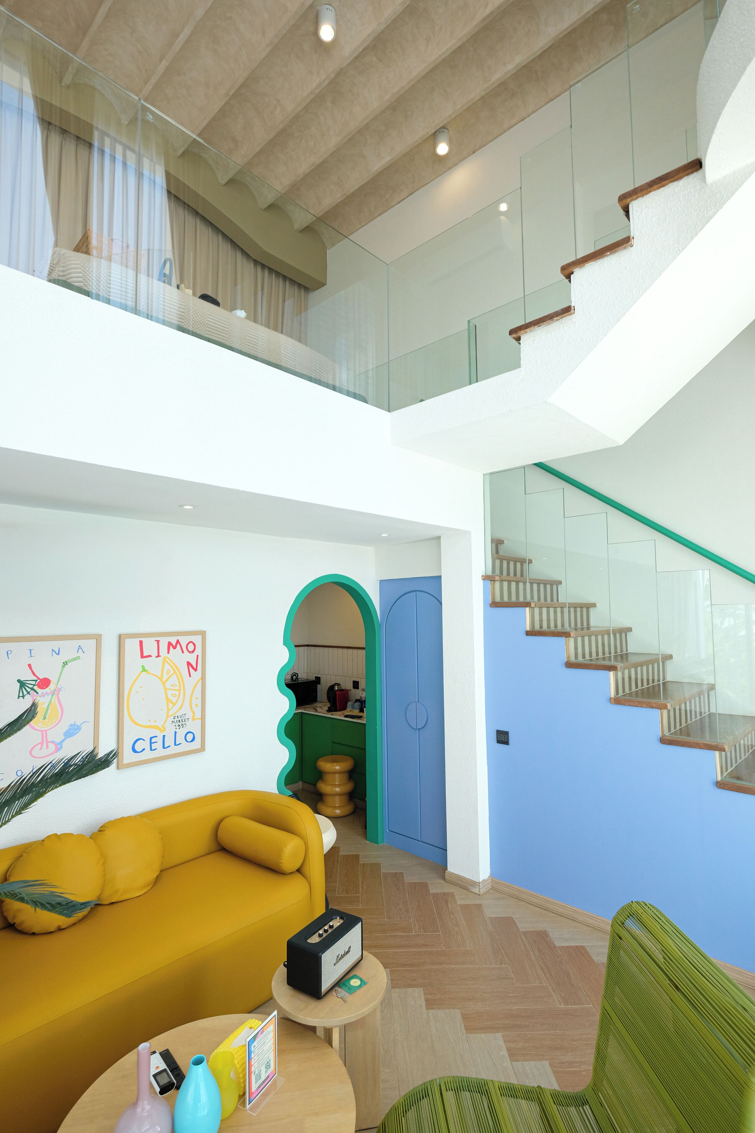 Interior moderno com sofá, uma mesinha, uma poltrona verde, escada com guarda-corrimão de vidro e uma porta azul.