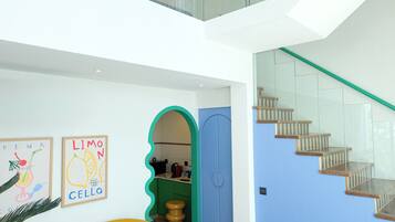 Interior moderno com sofá, uma mesinha, uma poltrona verde, escada com guarda-corrimão de vidro e uma porta azul.