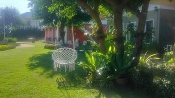 Um jardim bem cuidado com uma cadeira suspensa, plantas em vasos e gramado.