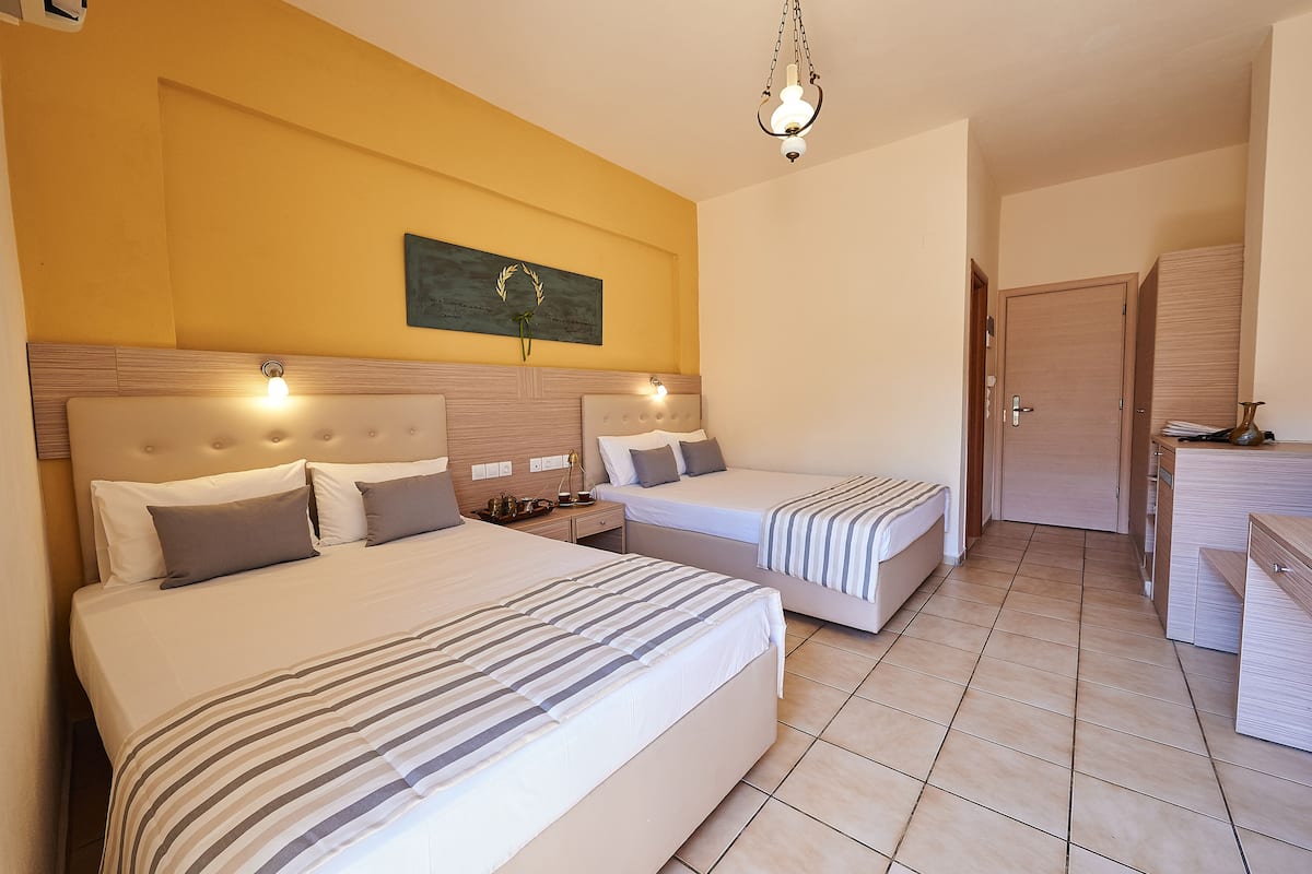 Quarto de hotel com duas camas, uma mesa de cabeceira, uma escrivaninha e um guarda-roupa.