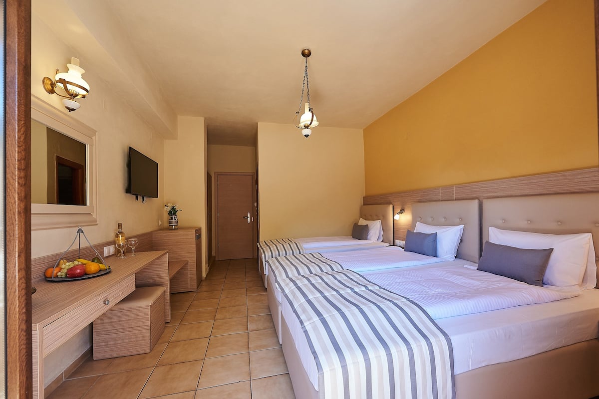 Quarto de hotel com duas camas, uma escrivaninha com um prato de frutas, uma televisão e um espelho.