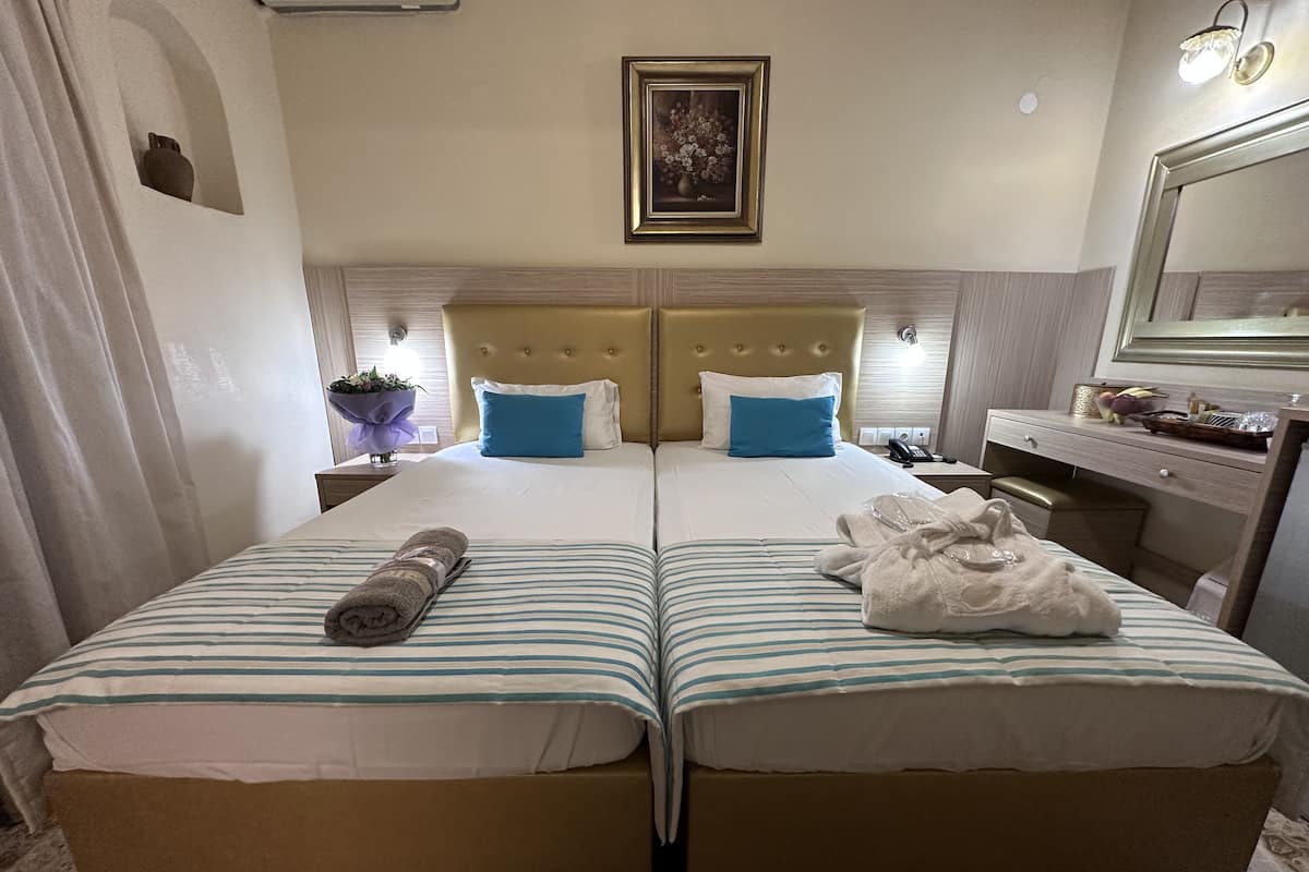 Uma cama de casal com duas almofadas, uma mesa de cabeceira com abajur e um espelho.