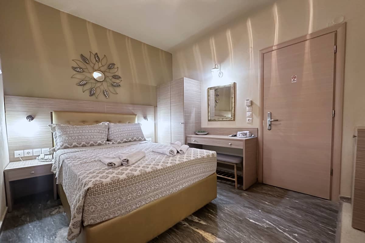 Quarto bem arrumado com cama, mesa de cabeceira, cômoda, espelho e porta.