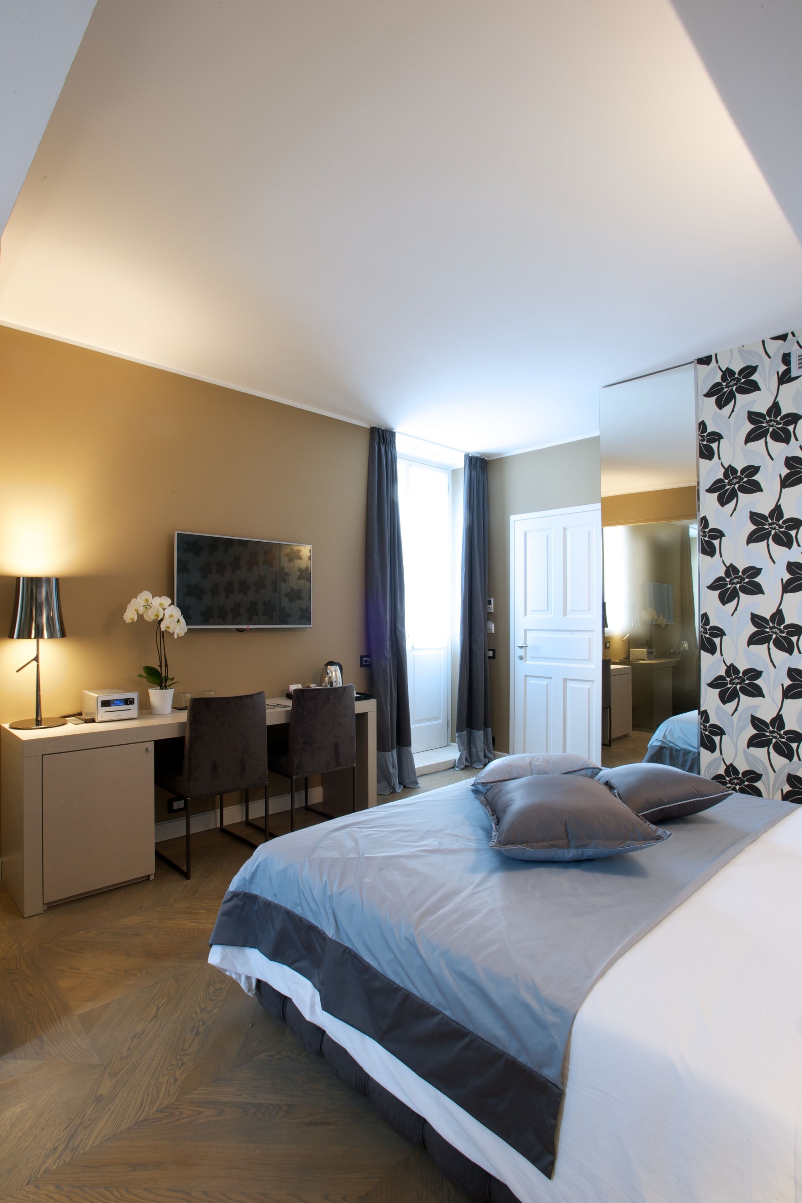 Quarto de hotel com cama, escrivaninha, cadeira e televisão na parede.