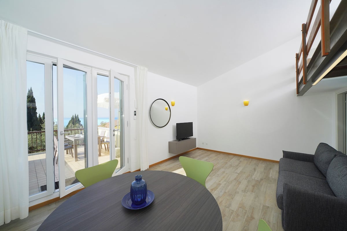 Uma sala de estar moderna com uma mesa de jantar, um sofá, uma televisão e uma varanda com vista.