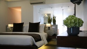Quarto de hotel moderno com uma cama, mesas de cabeceira, espelho e planta em vaso.