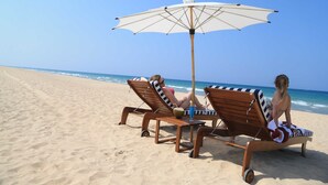 Duas cadeiras de madeira para relaxar com almofadas listradas e um grande guarda-sol numa praia de areia.