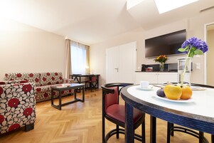 Sala moderna com sofá, mesa de jantar e cadeiras. Uma TV de tela plana está fixada na parede.
