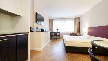Quarto de hotel com cama, escrivaninha, cadeira, televisão e janela com cortinas.