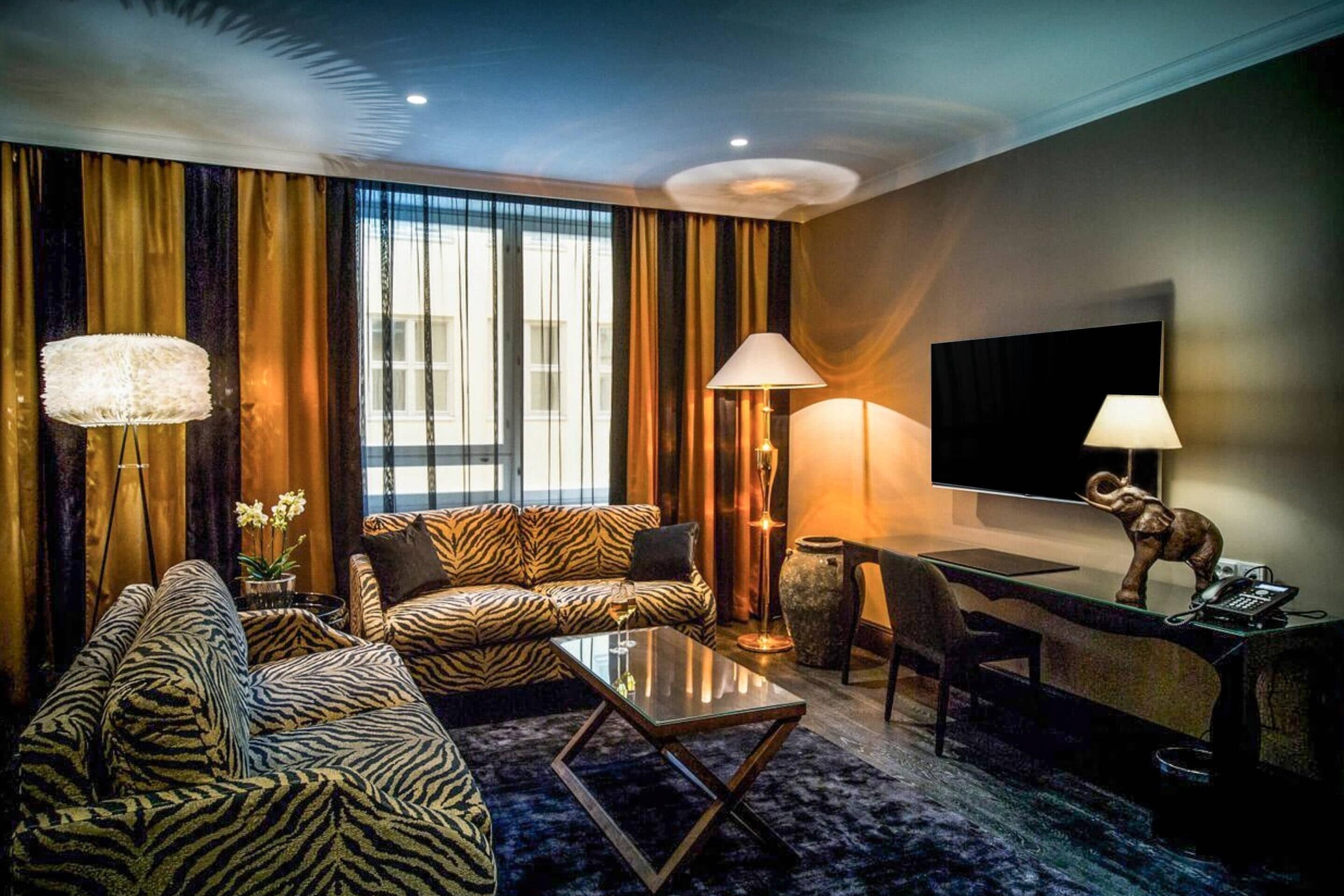 Quarto de hotel moderno com sofá de padrão de zebra, mesa de centro de vidro, escrivaninha com luminária e televisão de tela plana fixada na parede.
