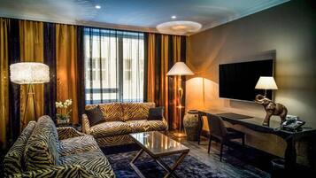Quarto de hotel moderno com sofá de padrão de zebra, mesa de centro de vidro, escrivaninha com luminária e televisão de tela plana fixada na parede.
