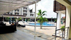 Uma área de piscina com espreguiçadeiras e guarda-sóis, um espaço de estar coberto e vista para a piscina.