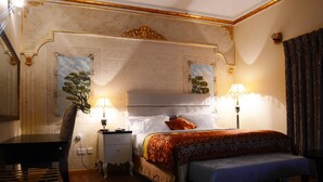 Quarto de hotel com cama, luminárias laterais, escrivaninha e uma cadeira.