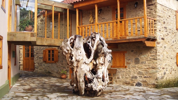 Um edifício de pedra com telhado de telhas vermelhas, varandas de madeira e um toco grande no pátio.