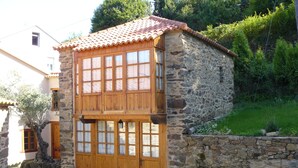 Um edifício de pedra com porta e janelas de madeira, cercado por vegetação.