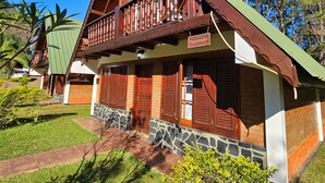 Uma casa de madeira tradicional com varanda, base de pedra e telhado verde.
