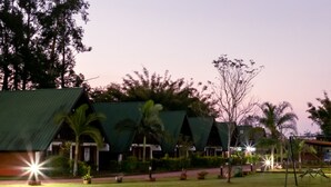 Um edifício com telhado verde e várias janelas, cercado por uma área gramada com árvores e plantas.