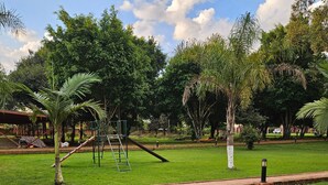 Uma área ajardinada com parque infantil, incluindo escorrega e estruturas de escalada.