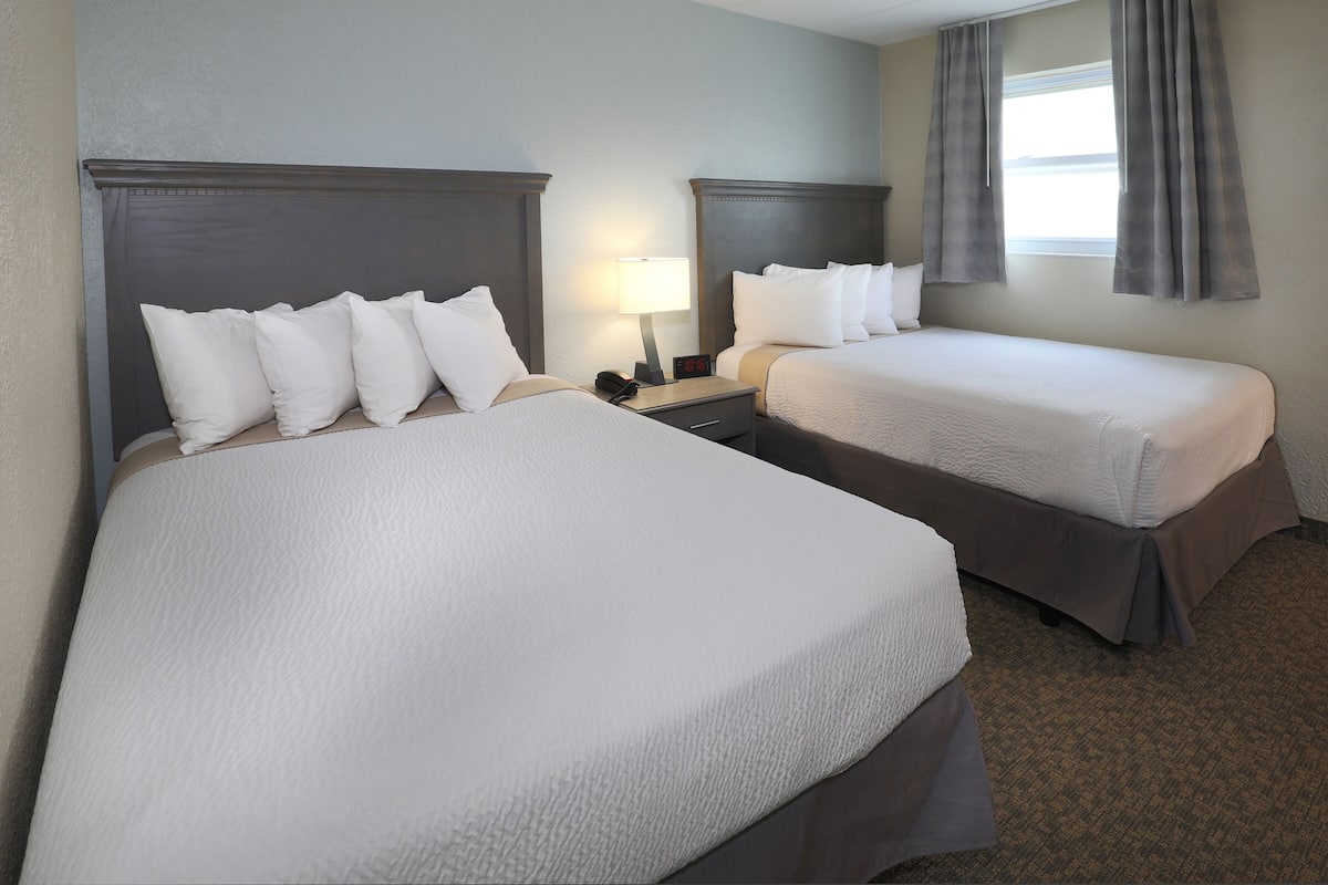 Quarto de hotel com duas camas, uma mesa de cabeceira com abajur e uma janela com cortinas.