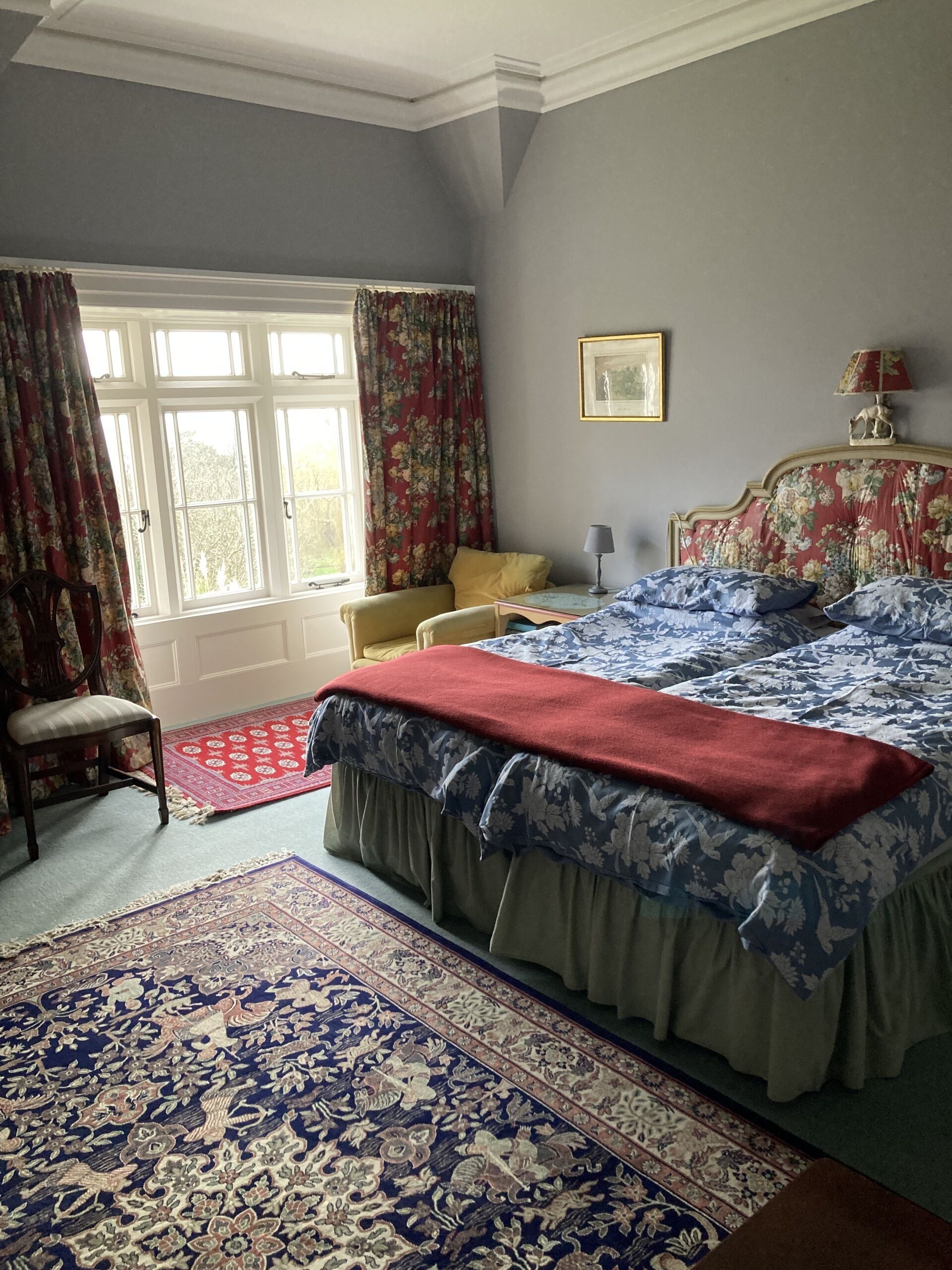 Quarto com uma cama grande, uma cadeira, janela com cortinas e um tapete.