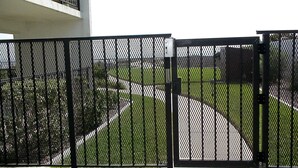 Uma entrada protegida por grades de metal, um caminho de acesso pavimentado e uma área gramada.