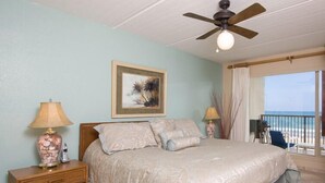 Quarto com cama, duas mesas de cabeceira, ventilador de teto, quadro emoldurado e vista para a praia.