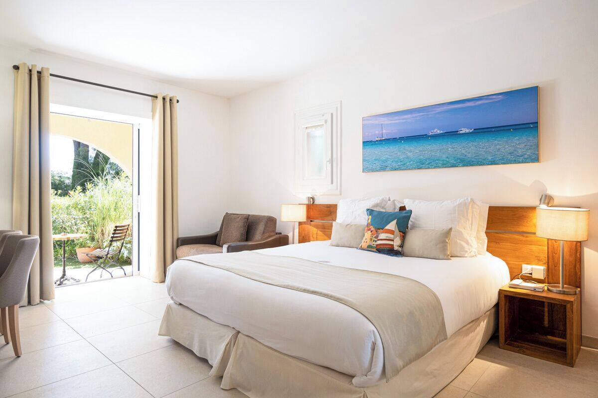 Quarto de hotel com uma cama grande, uma escrivaninha, uma cadeira, uma mesa de cabeceira com abajur e uma pintura com vista para o mar.