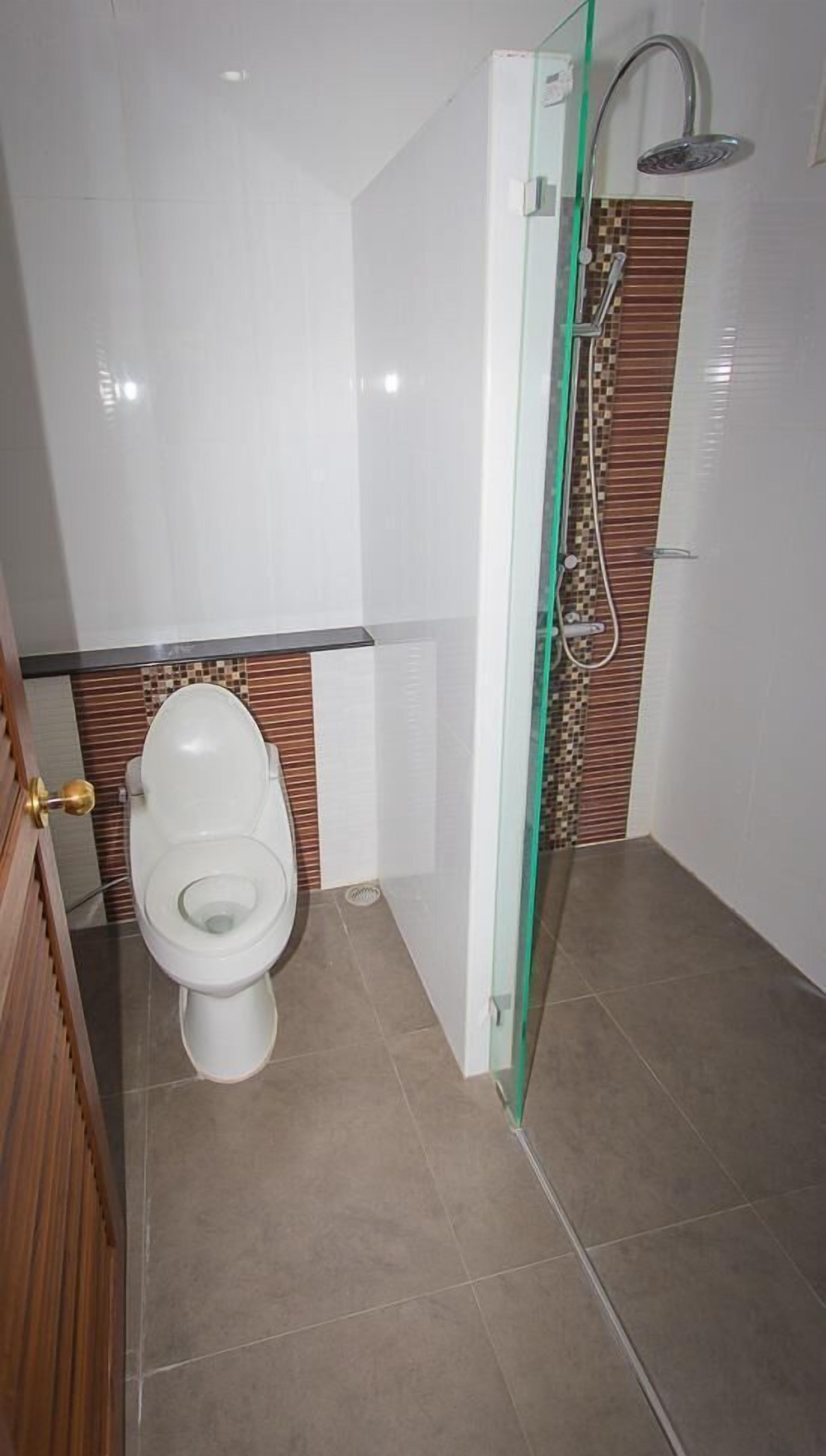 Casa de banho com sanita, chuveiro e divisória de vidro.