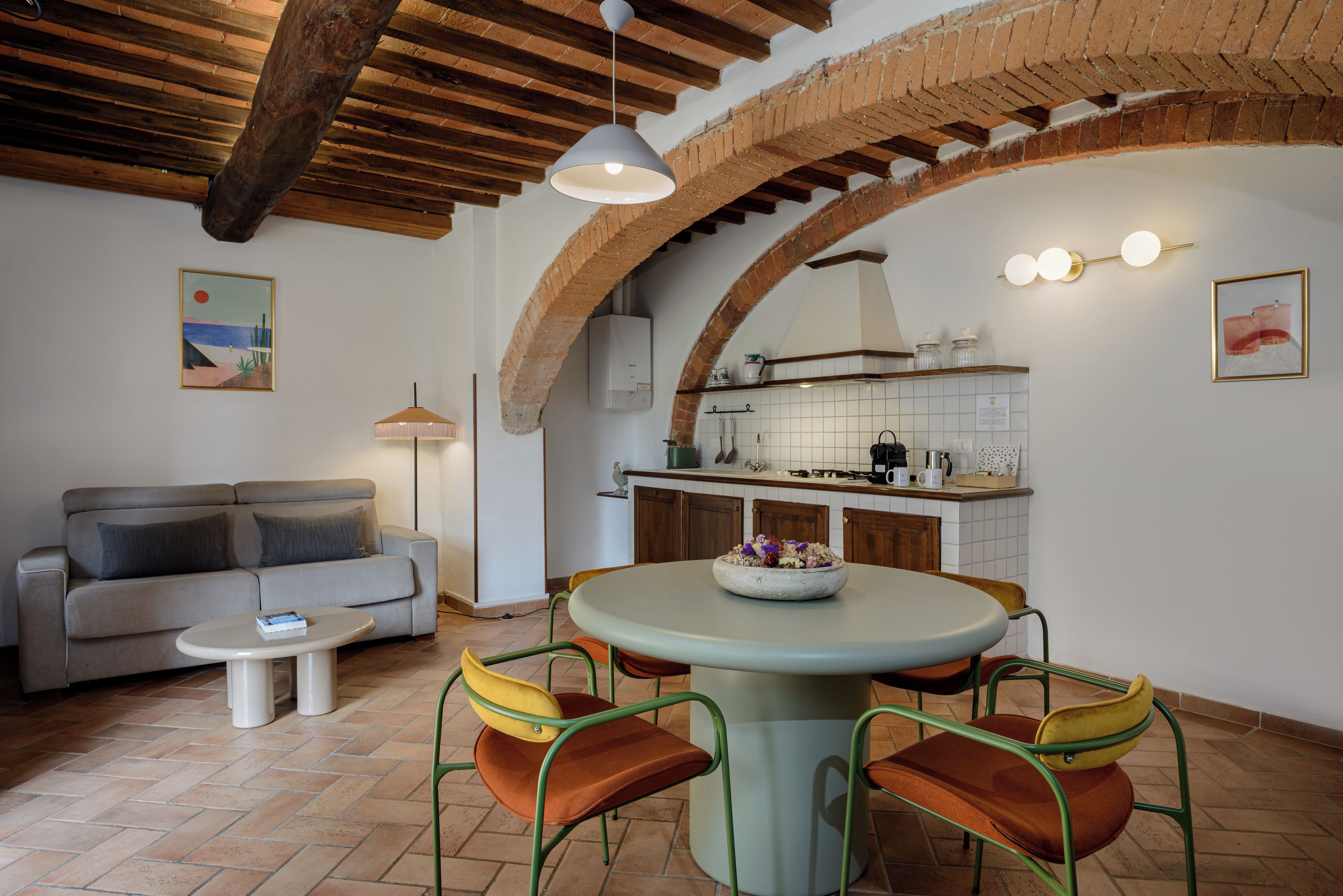 Uma sala de estar acolhedora com sofá, uma mesa redonda com cadeiras, uma cozinha com fogão e um lustre.