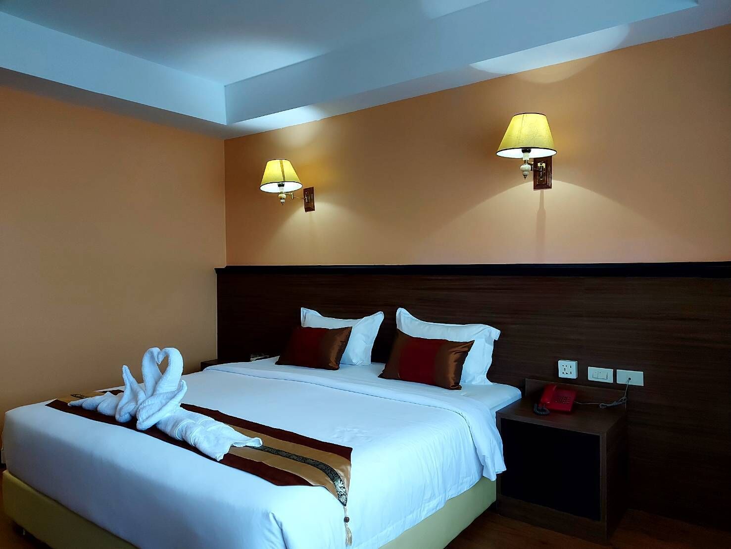 Quarto de hotel com uma cama grande, duas luminárias laterais, uma mesa de cabeceira com telefone e um aplique na parede.