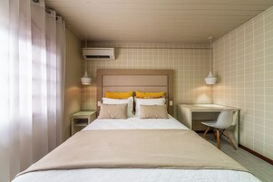 Quarto de hotel com cama, mesas de cabeceira, escrivaninha e ar condicionado.