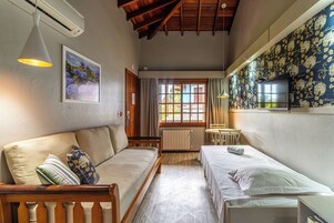 Quarto com teto de madeira, um sofá, uma cama, uma mesinha e uma televisão fixada na parede.