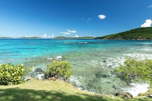 Vista costeira deslumbrante com águas azul-turquesa, vegetação verde e colinas ao longe.