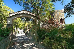 Uma trilha de pedra leva a um edifício com torre arredondada e entrada em arco.