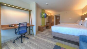 Quarto de hotel com escrivaninha, cadeira, cama e televisão na parede.