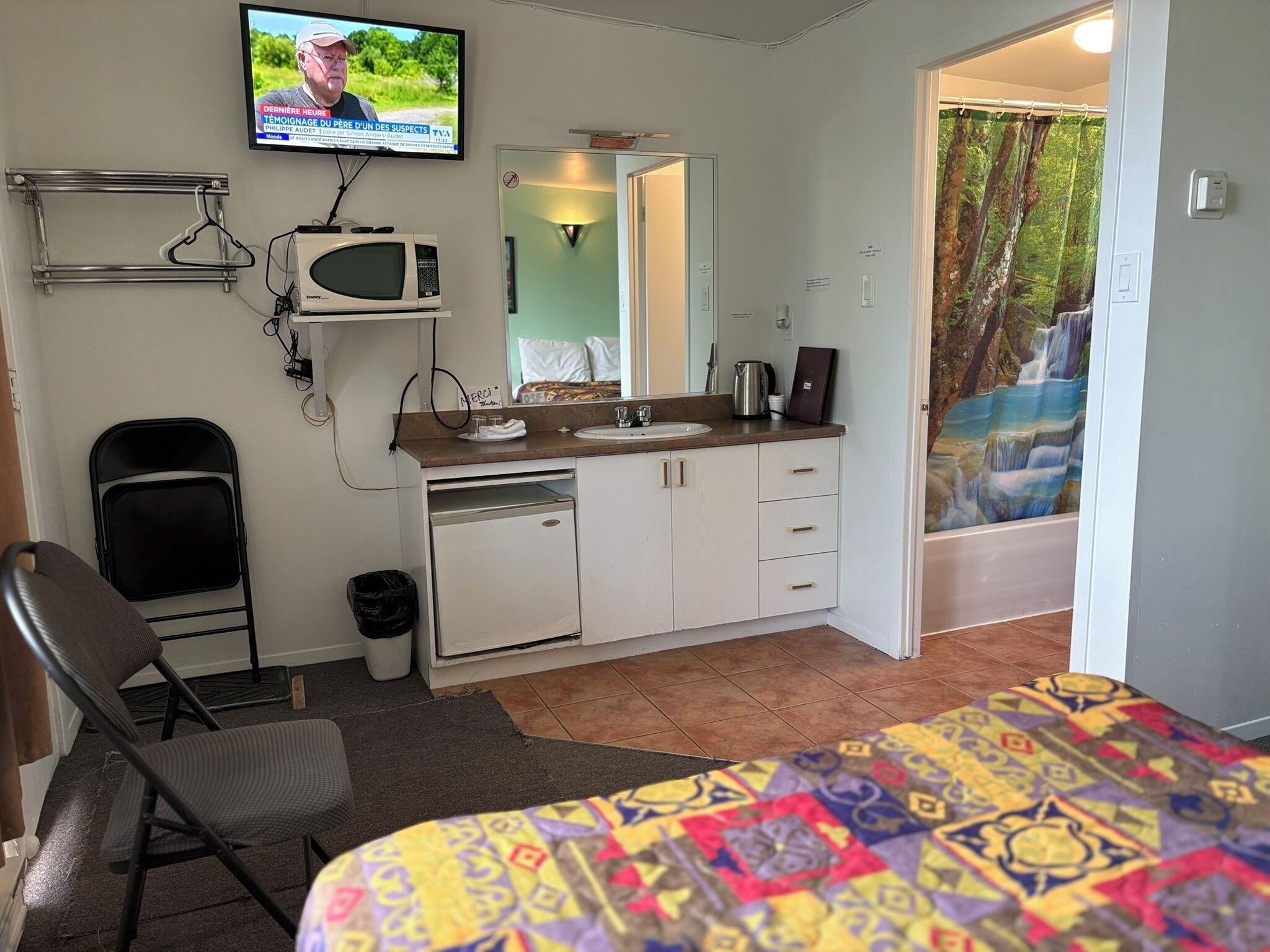 Quarto de hotel compacto com cama, pequena área de estar, cozinha compacta e banheiro.