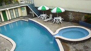 Piscina com uma pequena banheira de hidromassagem, rodeada por cadeiras de descanso brancas e guarda-sóis verdes e brancos.