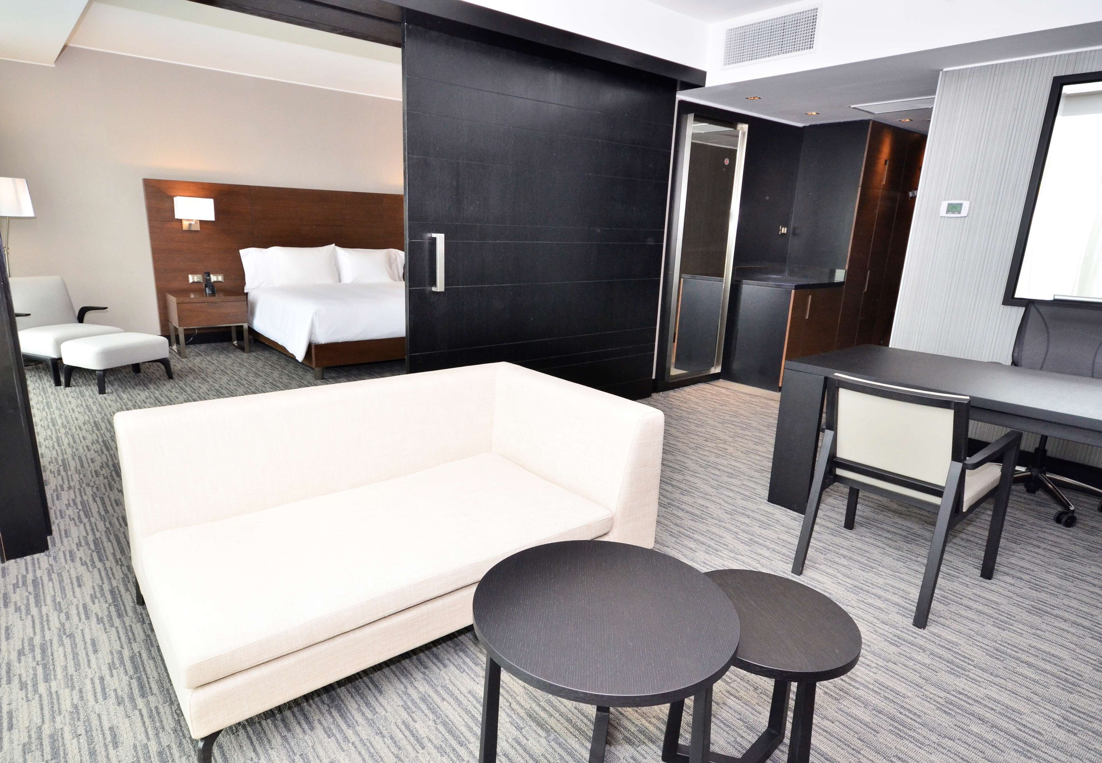 Quarto de hotel com cama, sofá, duas mesinhas, escrivaninha e espelho.